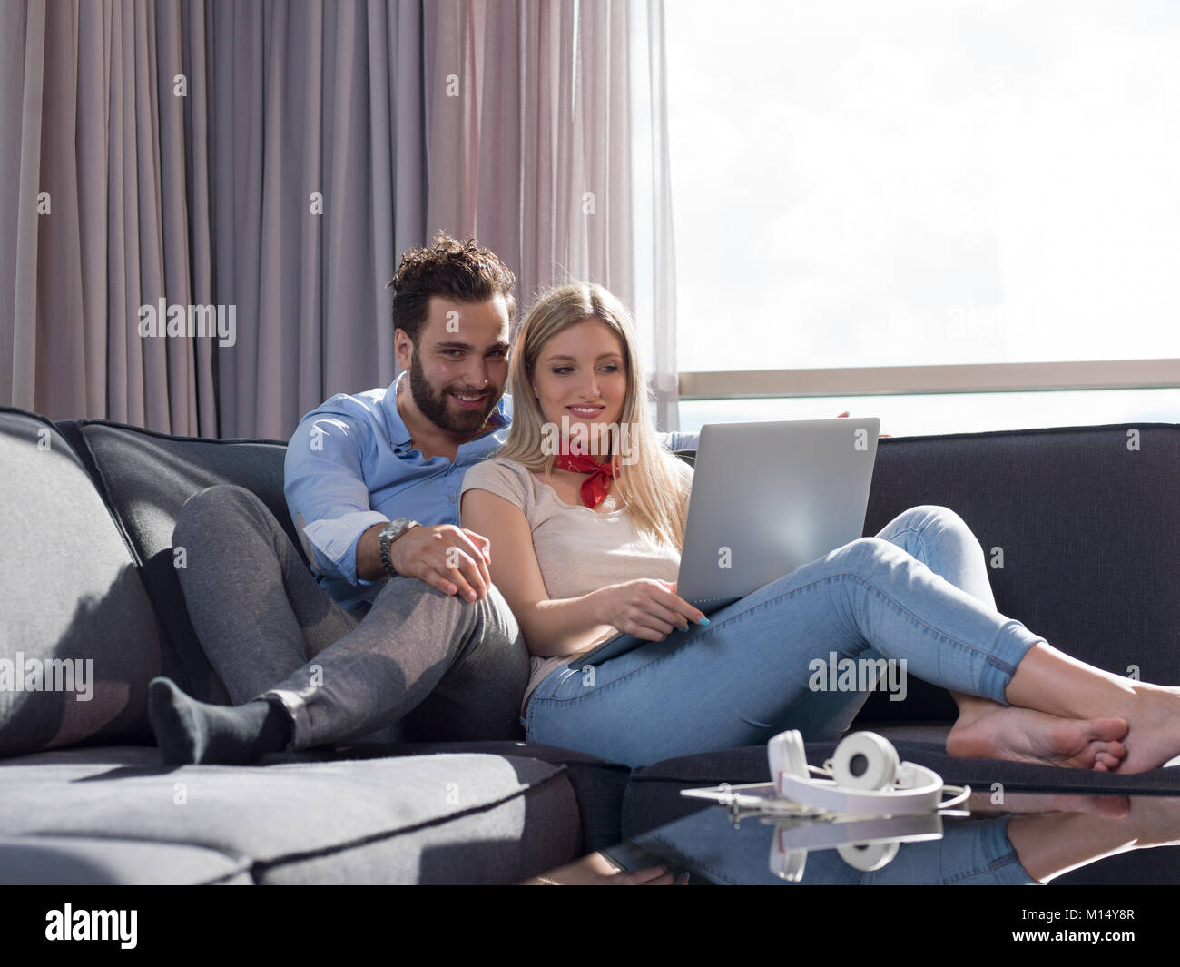 Young couple relaxing at luxury home using laptop computer reading in ...