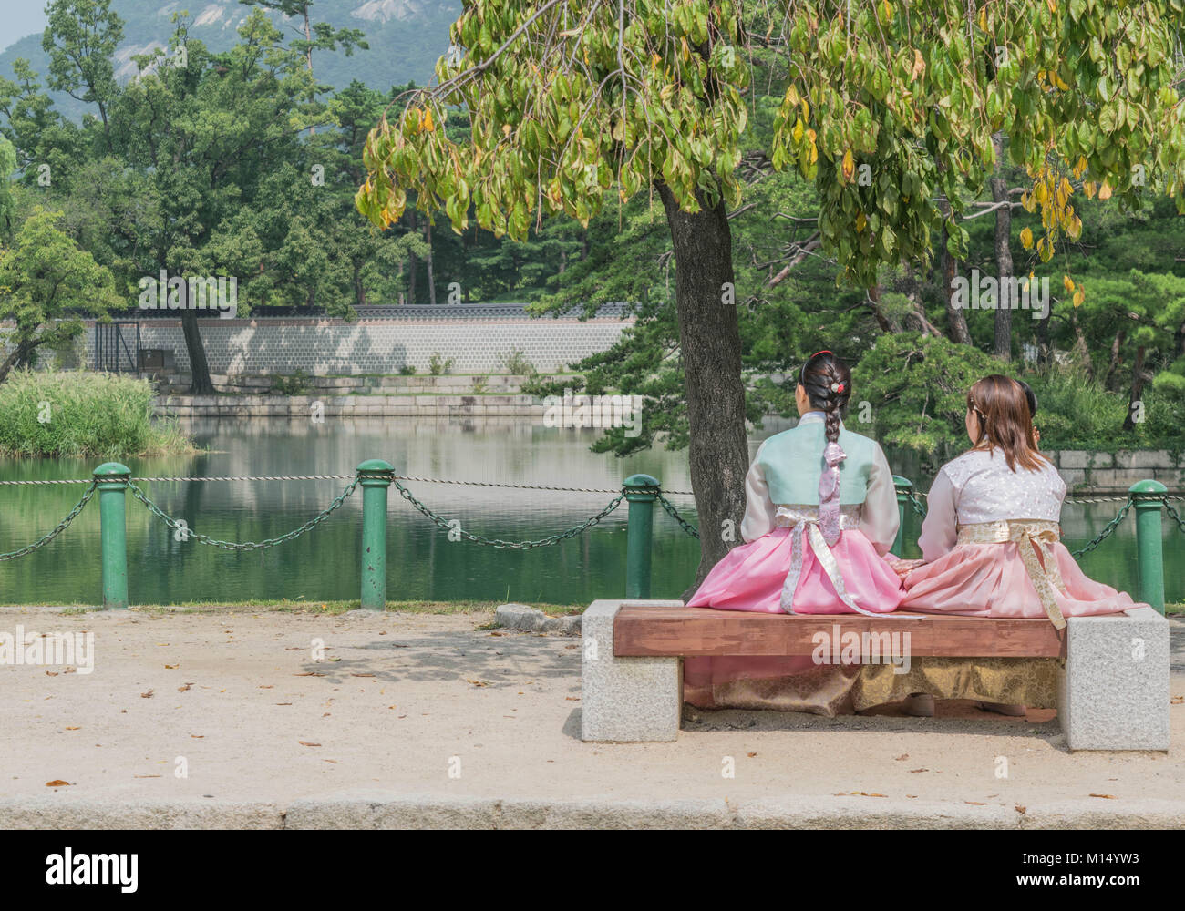 Two women in traditional Korean clothing sitting on a bench, enjoying a ...