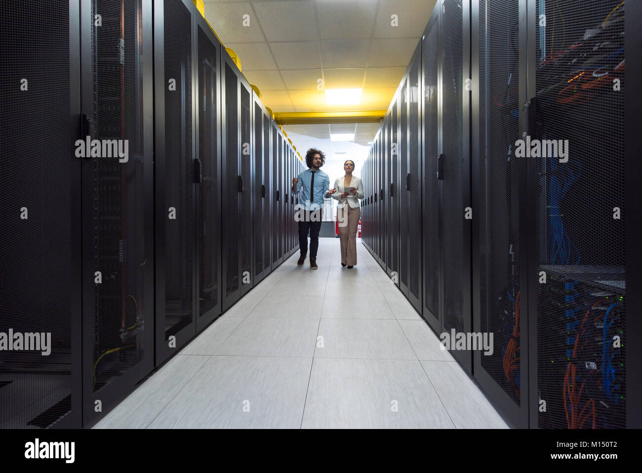 Young IT engineer showing working data center server room to female ...