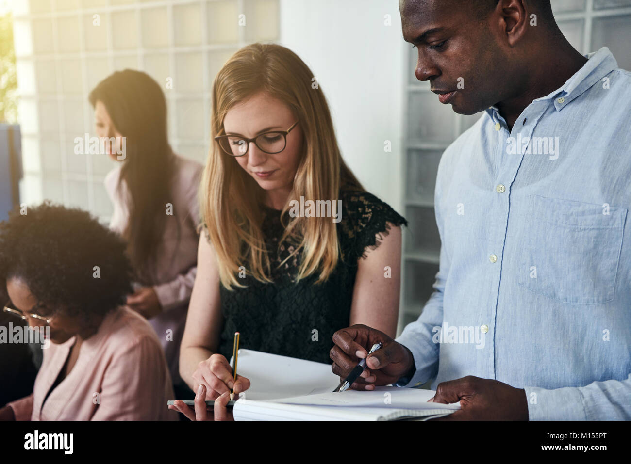 Two coworkers comparing notes while working together in a modern office ...