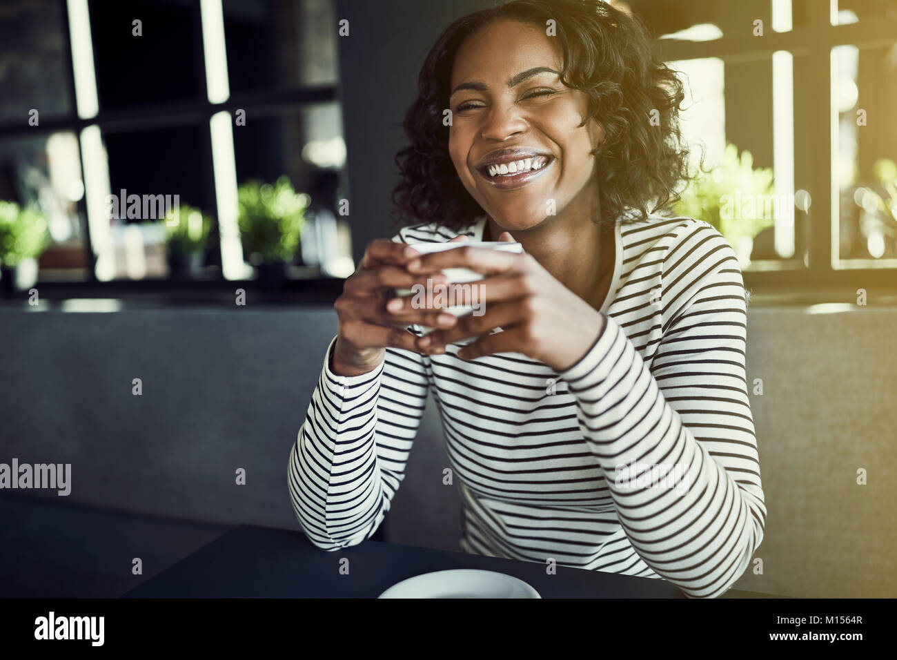 Young African woman laughing while sitting alone at a table in a cafe ...