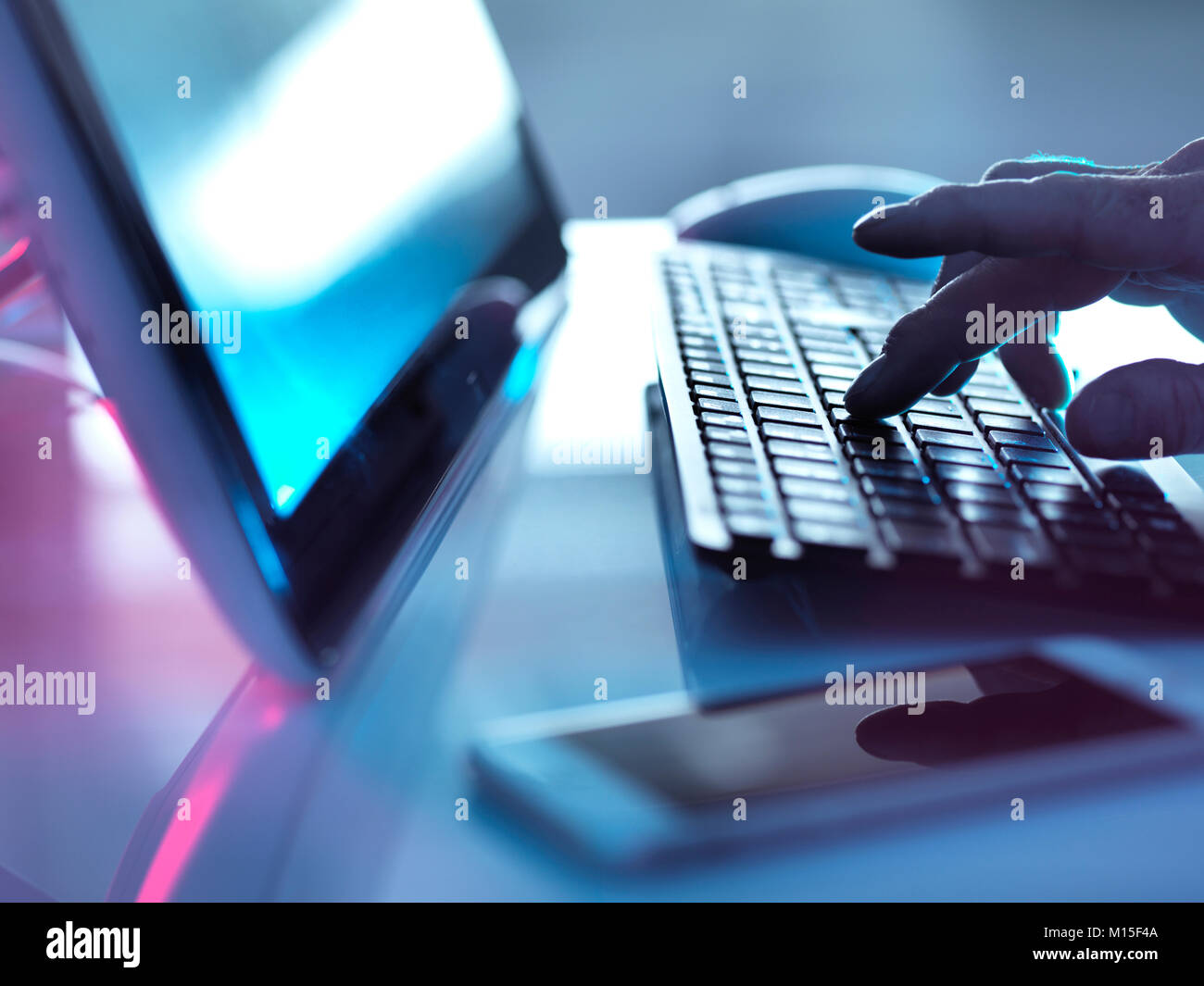 MODEL RELEASED. Computer use. Man working at PC with a mobile phone on ...