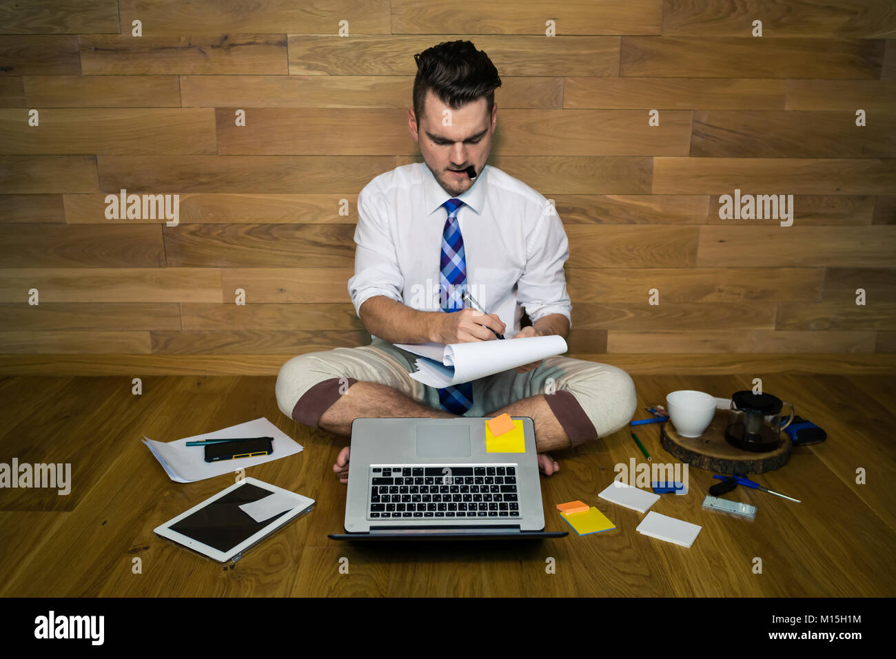 A barefoot businessman sits on the floor with a lot of gadgets. Serious ...