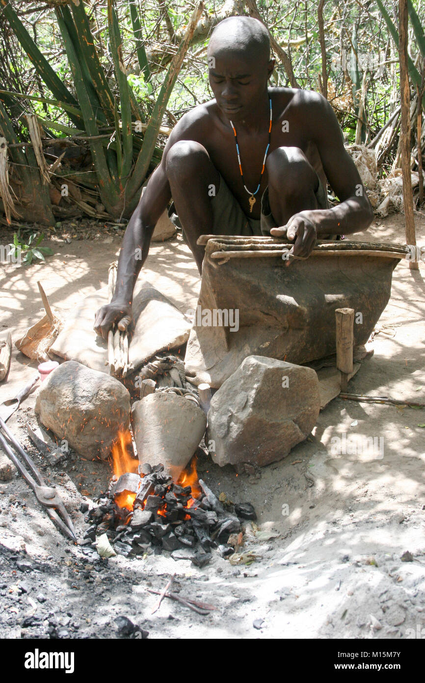 Datoga man prepares and lights the campfire using a goat skin bellows ...