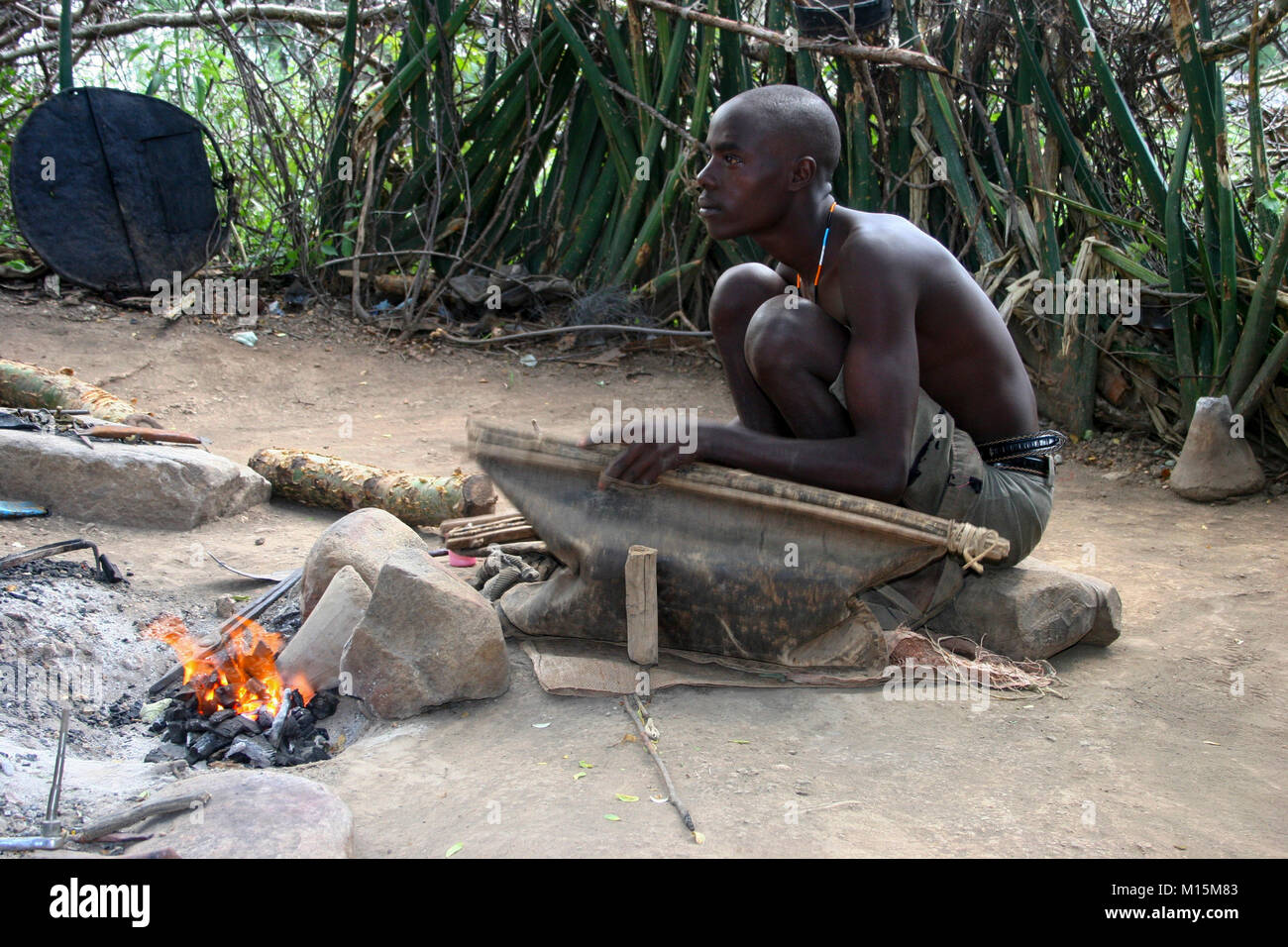 Datoga man prepares and lights the campfire using a goat skin bellows ...