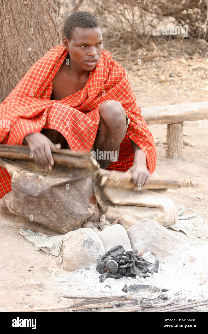 Datoga man prepares and lights the campfire using a goat skin bellows ...
