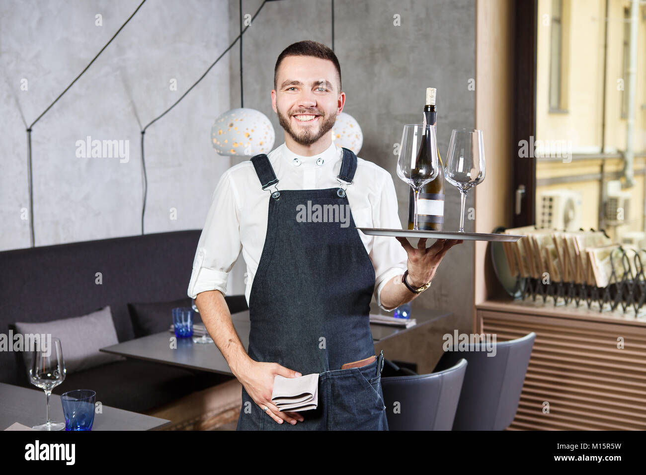 A young, handsome Caucasian waiter stands in the interior of the ...