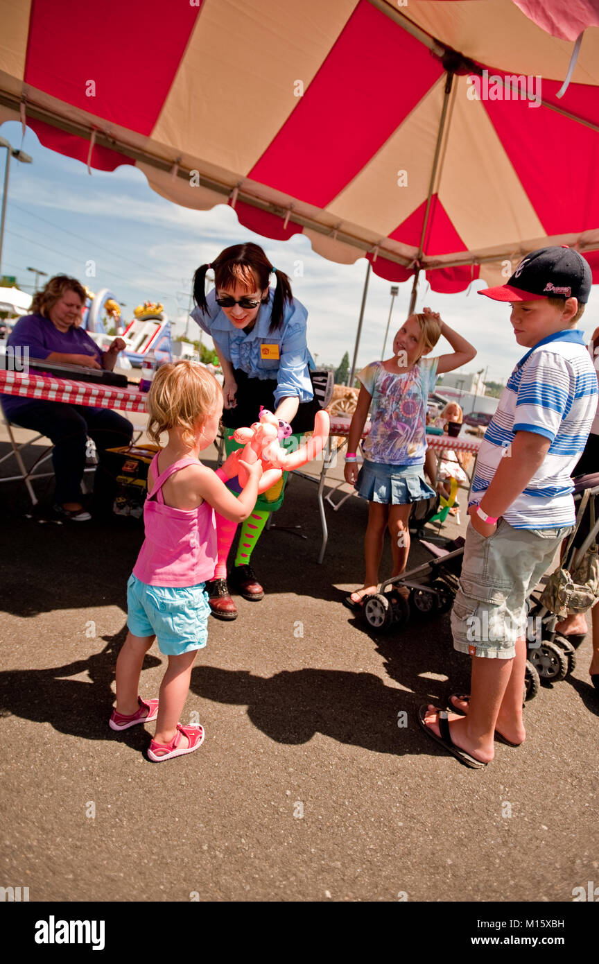 A female balloon artist handing out balloon animal to little kid Stock ...