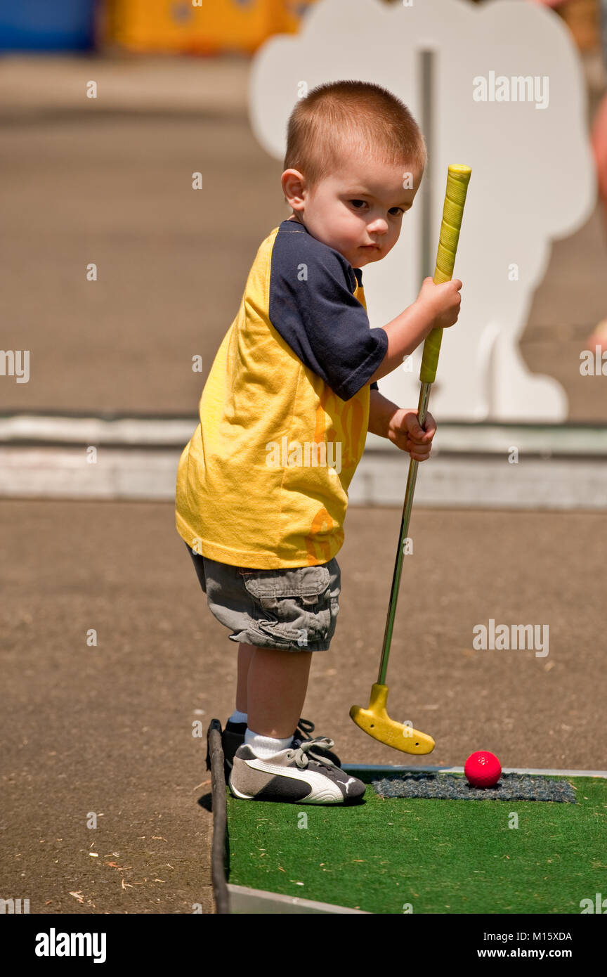 A serious little boy golfer was putting a red golf ball at a mini golf ...