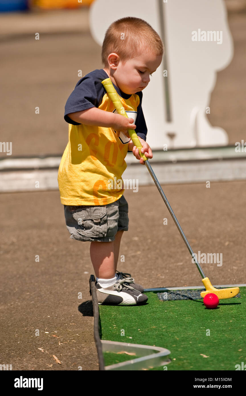 A serious little boy golfer was putting a red golf ball at a mini golf ...