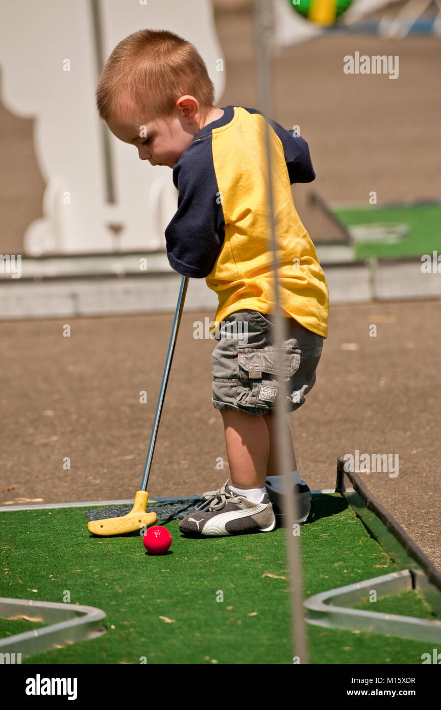 A serious little boy golfer was putting a red golf ball at a mini golf ...