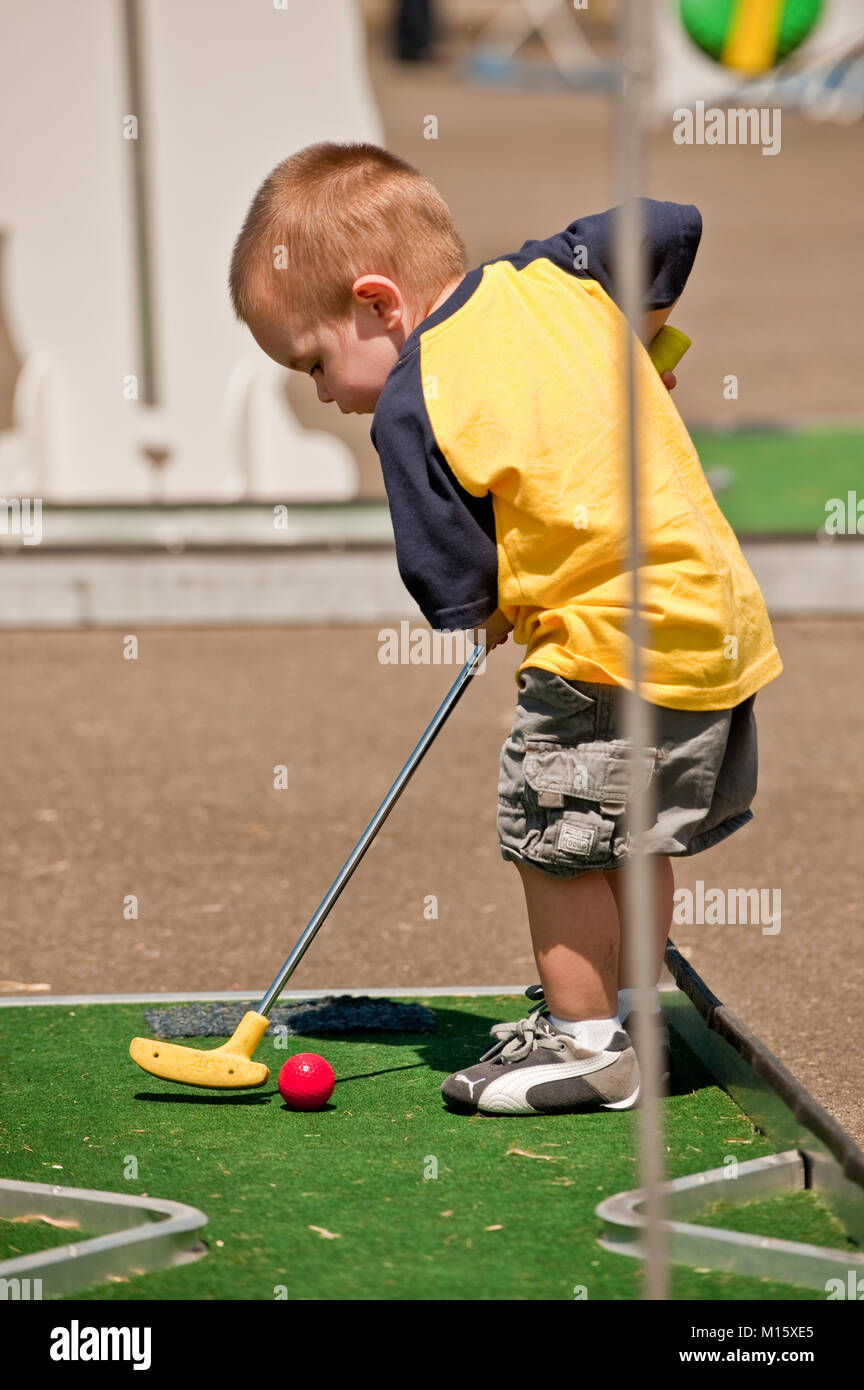 A serious little boy golfer was putting a red golf ball at a mini golf ...