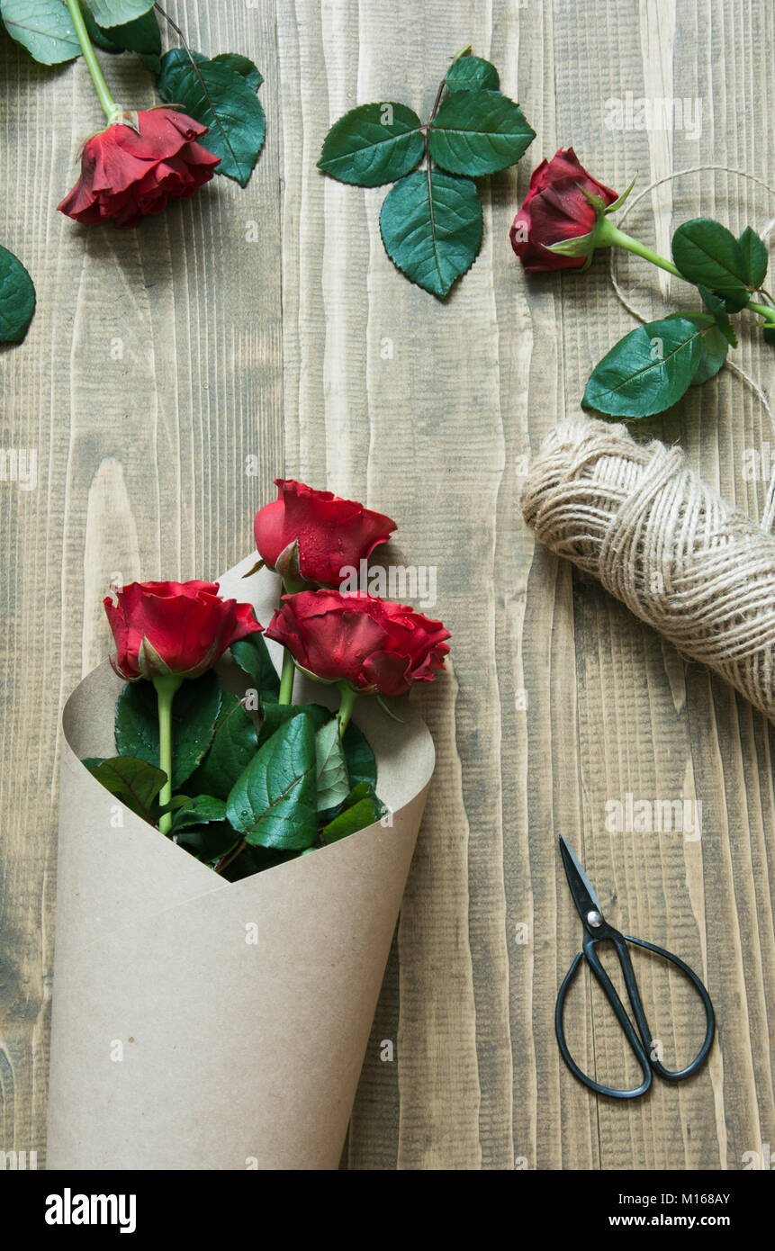 Florist making a red roses bouquet, wrapping in kraft paper on a wooden ...