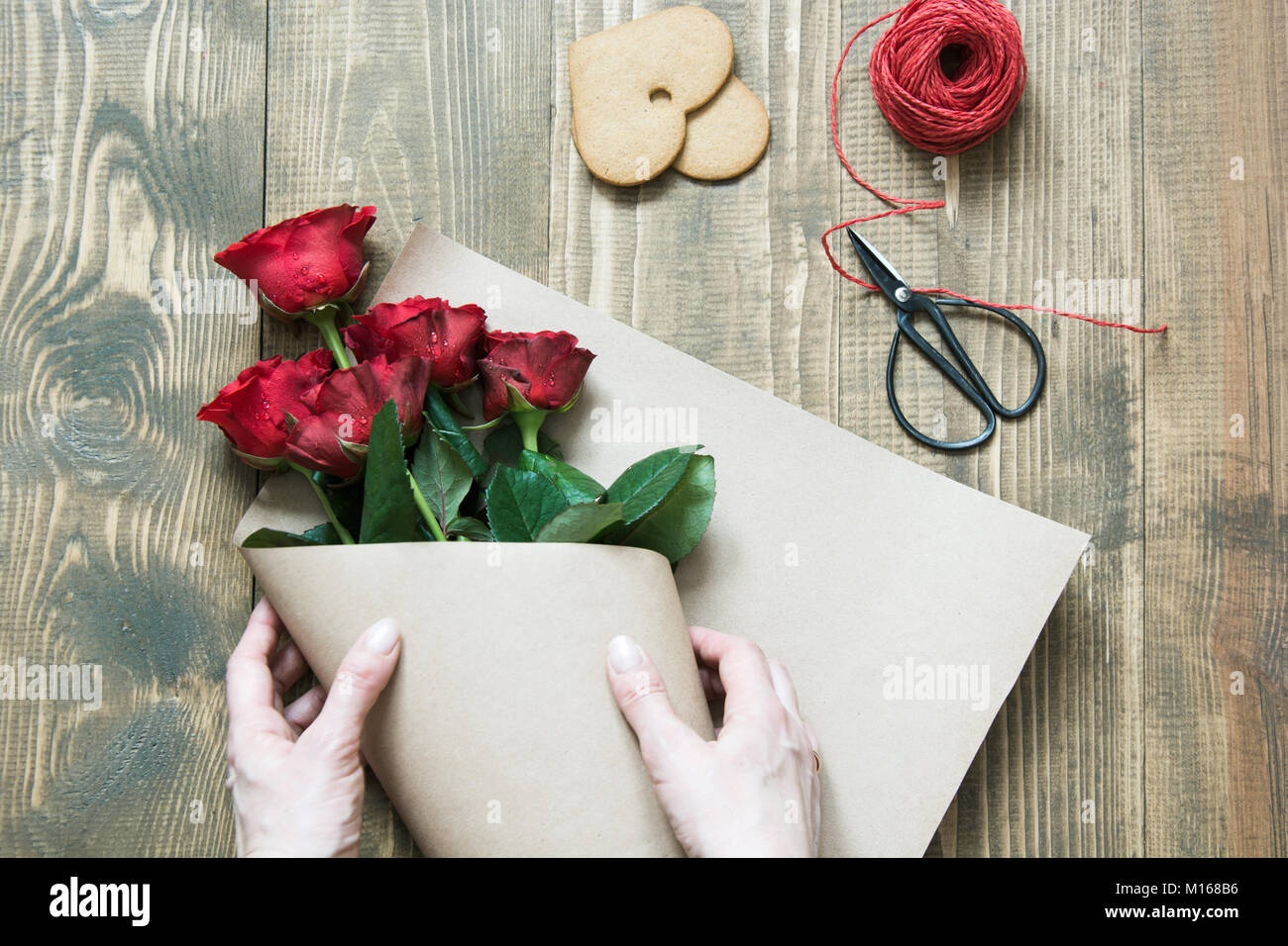 Florist making a red roses bouquet, wrapping in kraft paper on a wooden ...
