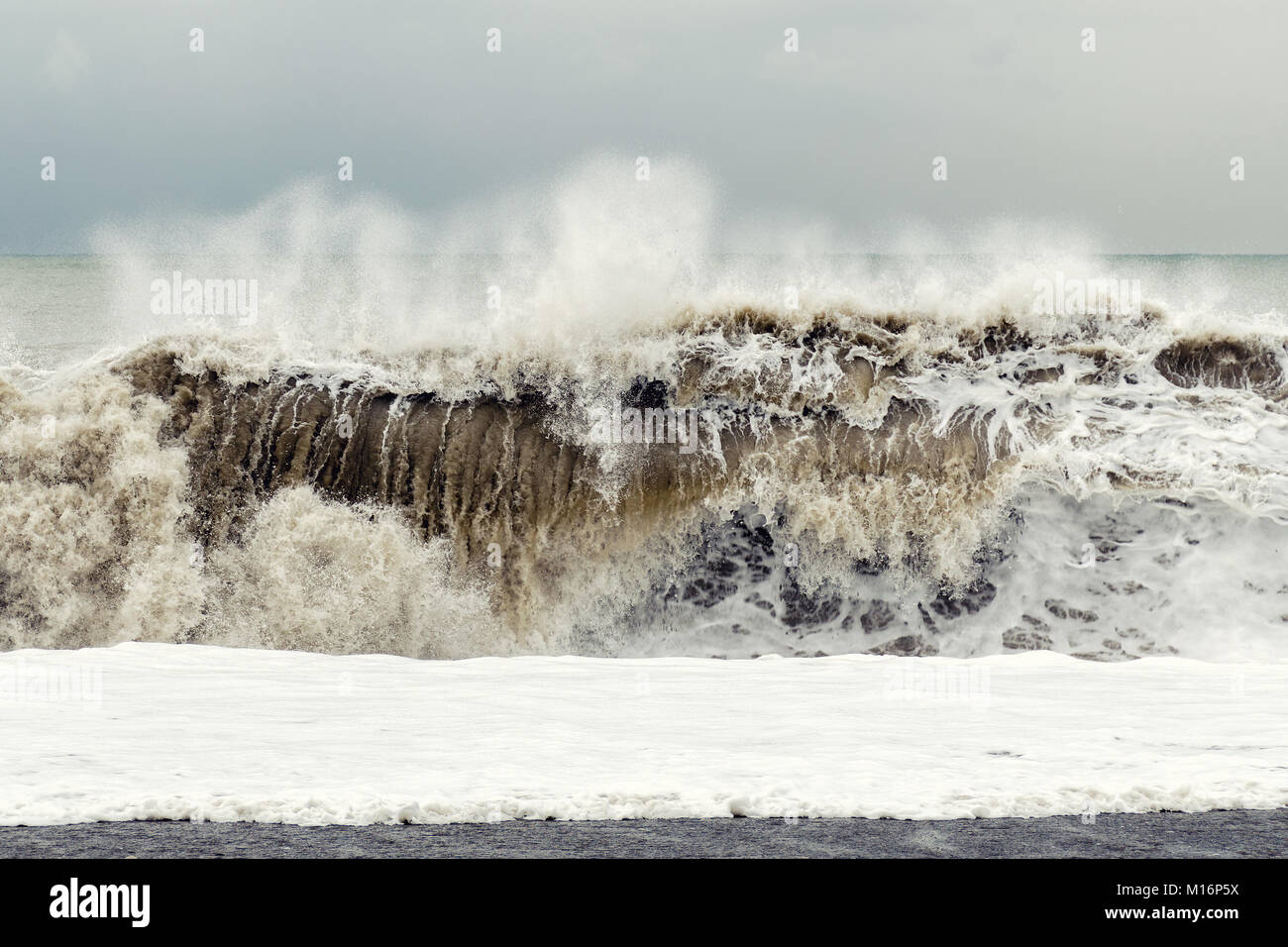 Storm on the sea - a big wave with sand and foam rises near the shore ...