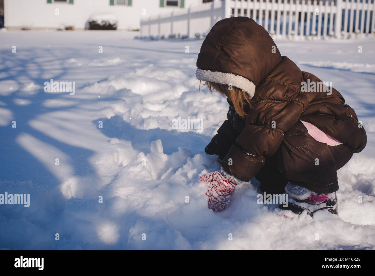 A 3-year old child wearing winter clothes, winter mittens, plays in the ...