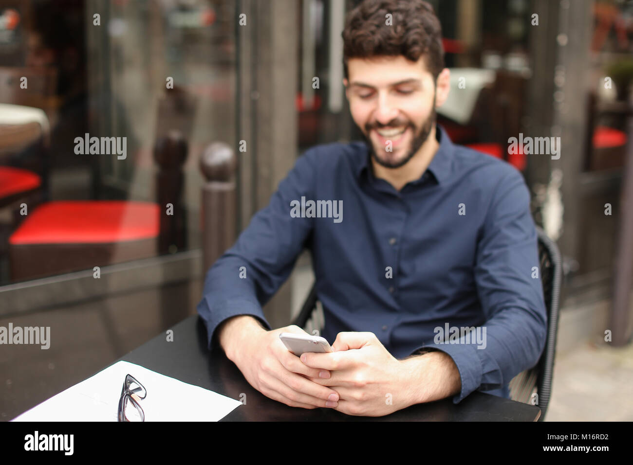 Happy man sitting at cafe table and chatting by smartphone with Stock ...
