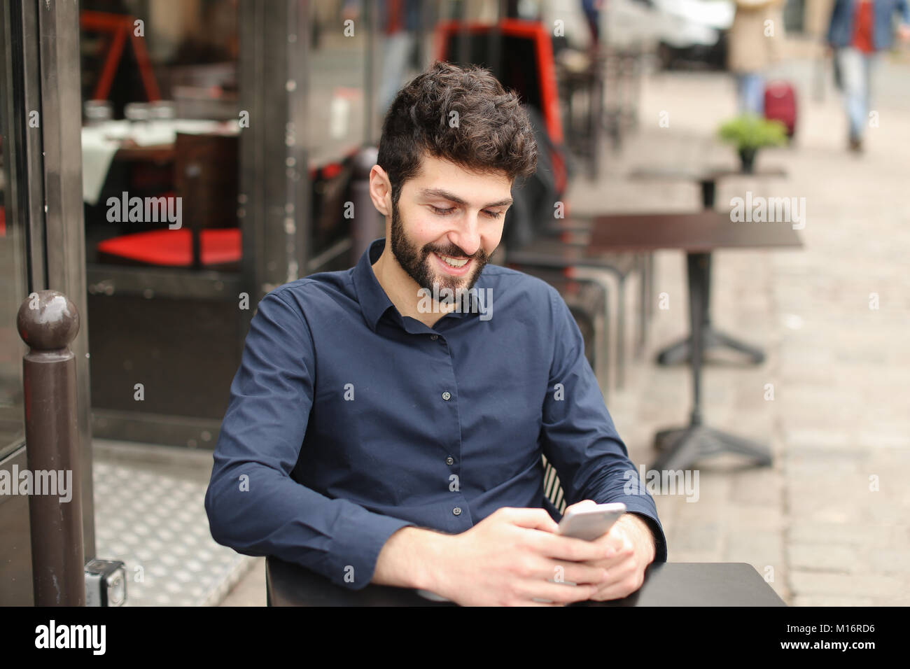 Happy man sitting at cafe table and chatting by smartphone with Stock ...