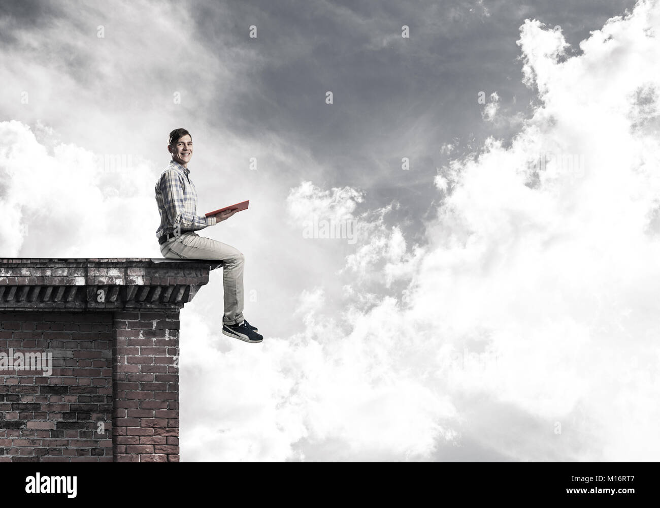 Man on roof edge reading book and cloudscape at background Stock Photo ...