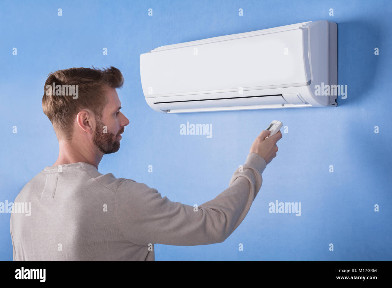 Rear View Of A Young Man Operating Air Conditioner Mounted On Blue Wall ...
