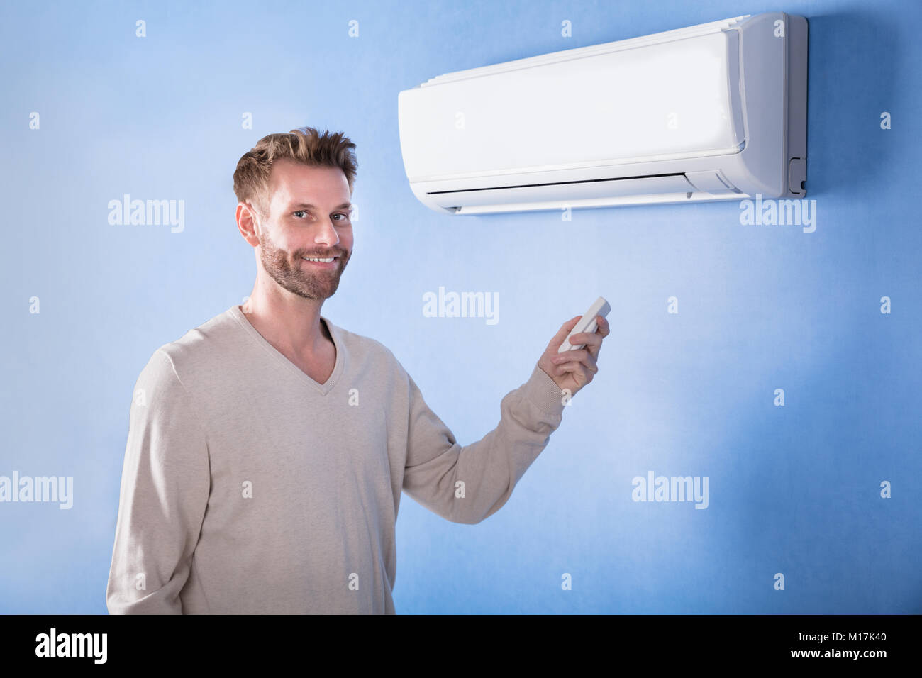 Happy Young Man Holding Remote Standing In Front Of Air Conditioner ...