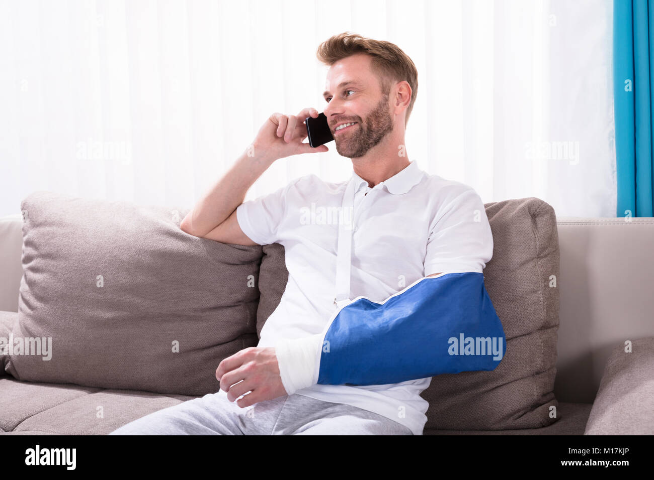 Young Man With Fractured Hand Sitting On Sofa Talking On Mobile Phone ...