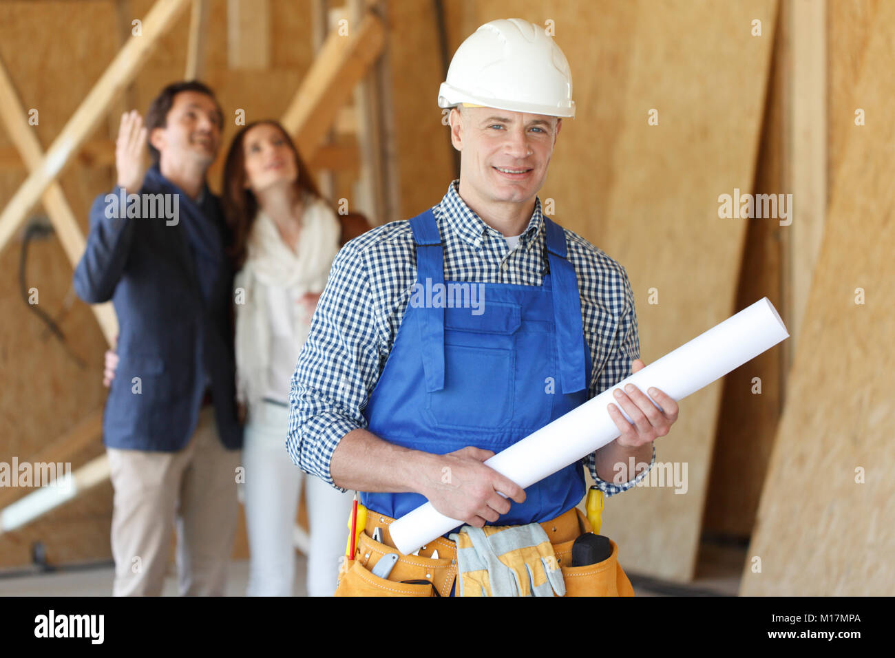 Worker shows house design plans to a young couple at construction site ...