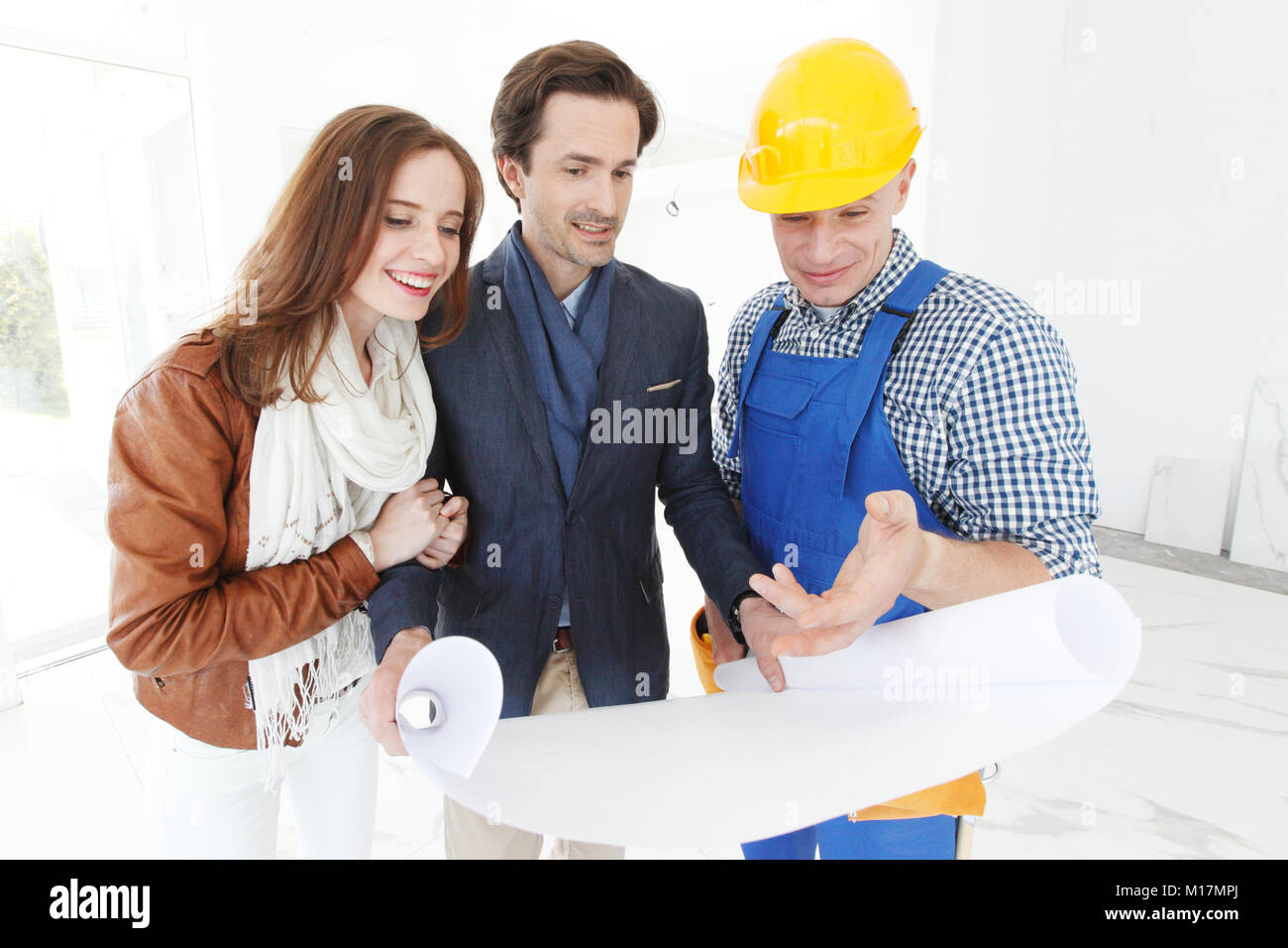 Worker shows house design plans to a young couple at construction site ...
