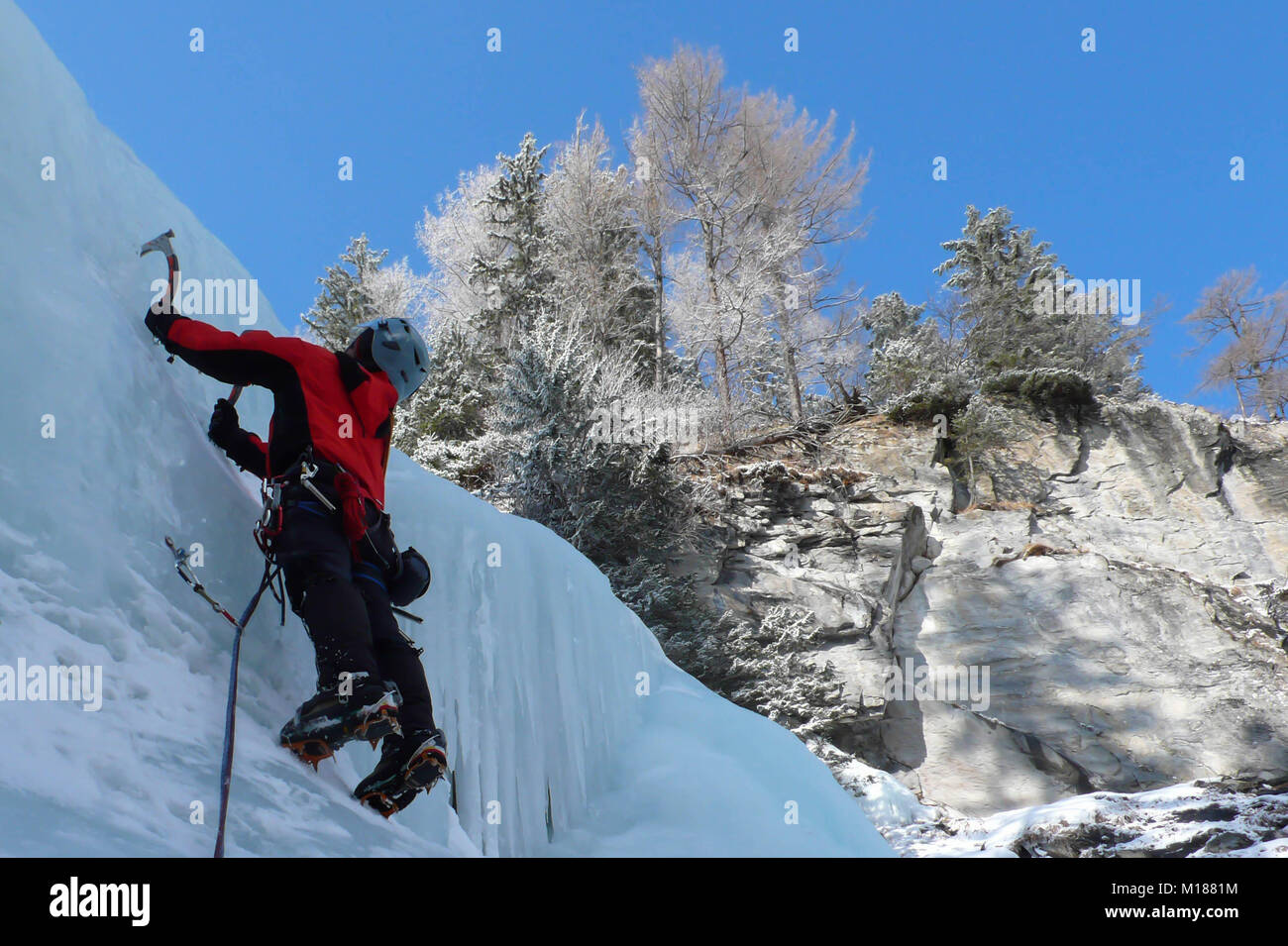 ice climber on a steep frozen waterfall in deep winter in the Alps in ...