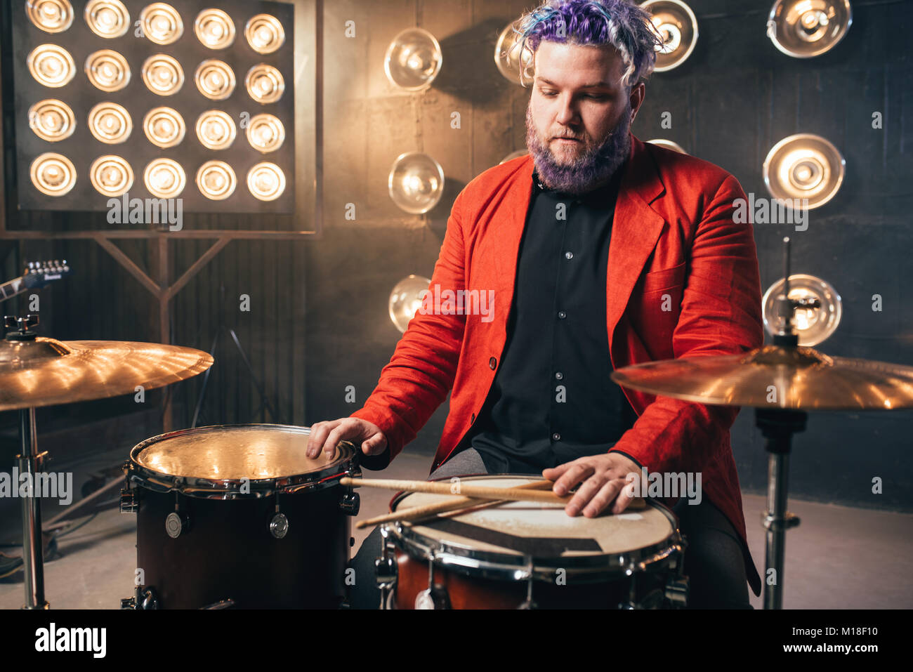 Bearded drummer in red suit, performing on the stage with lights ...