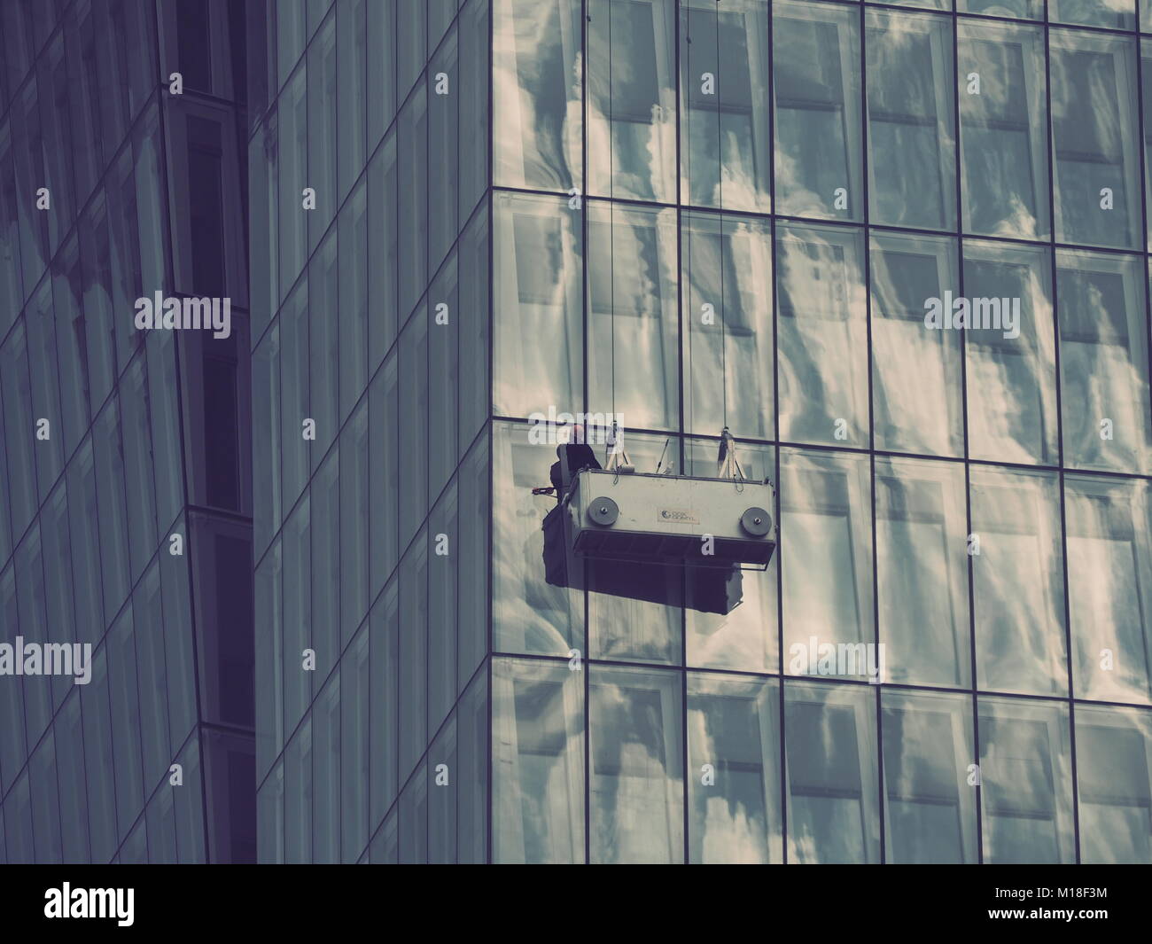 Cleaning worker hanging on cable lift outside skyscraper facade with a ...
