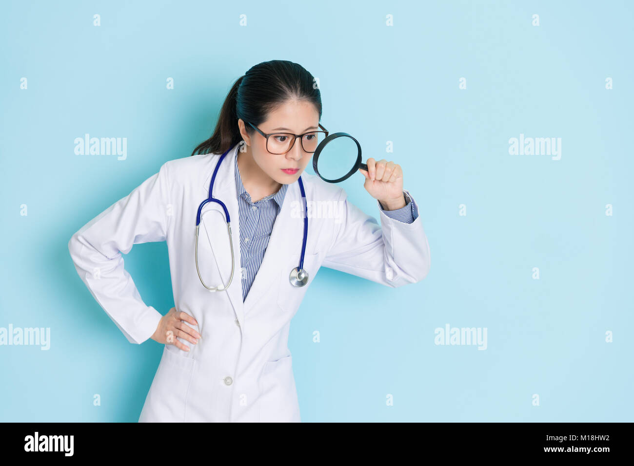 confident pretty female doctor standing in blue background looking down ...