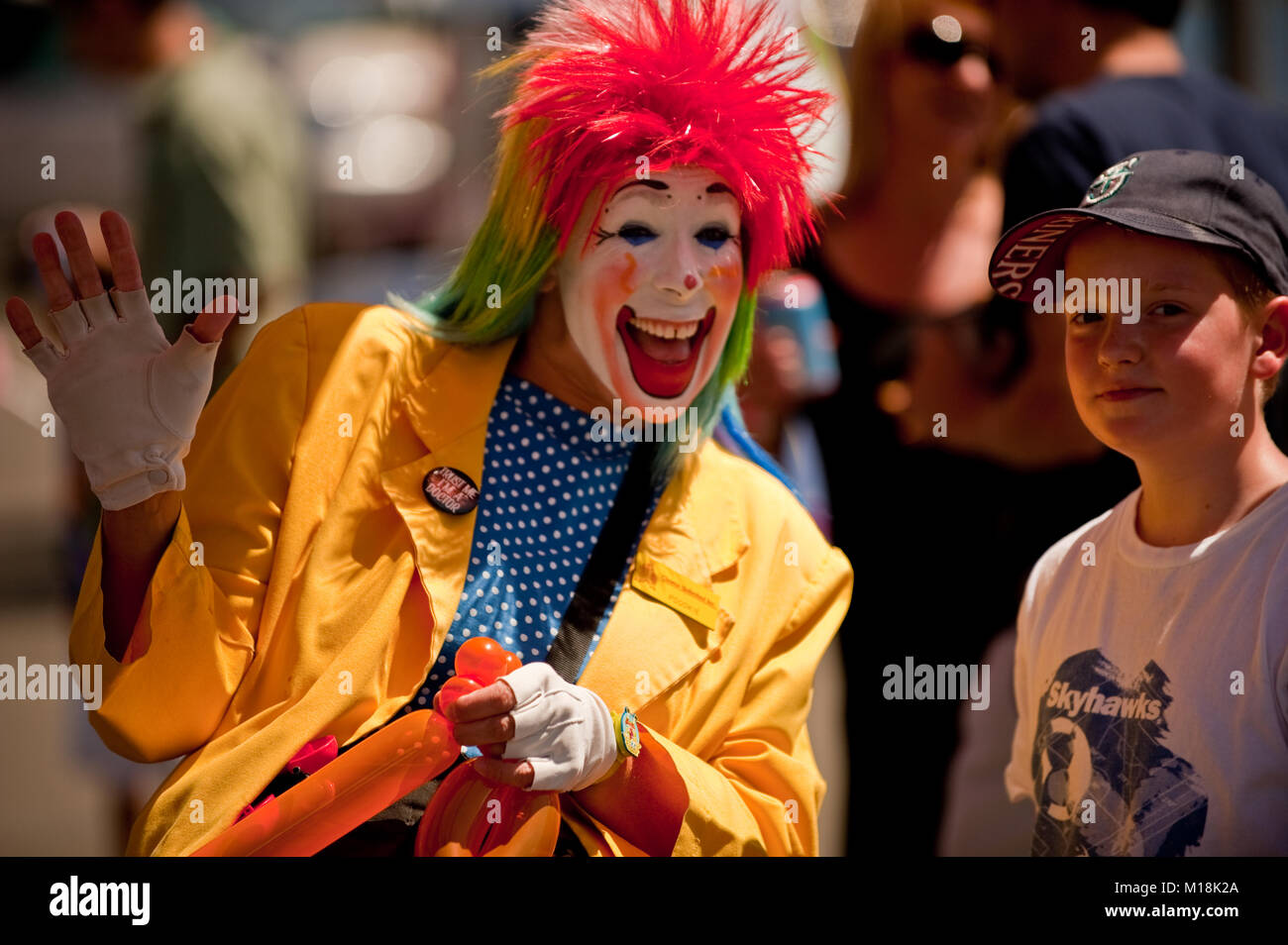 A young boy and a clown with colorful hairs and face in a yellow jacket ...