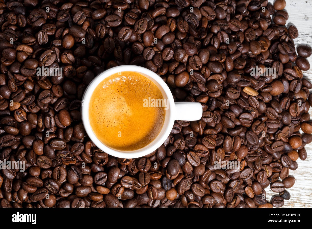 white cup of coffee, just done, on roasted coffee beans from top, just ...