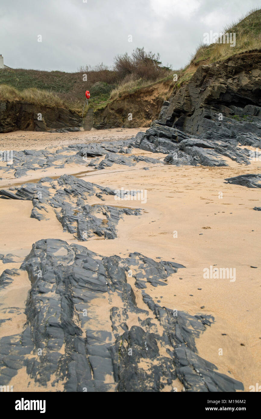 A view of a rocky Cornish beach with steps to a red life preserver belt ...
