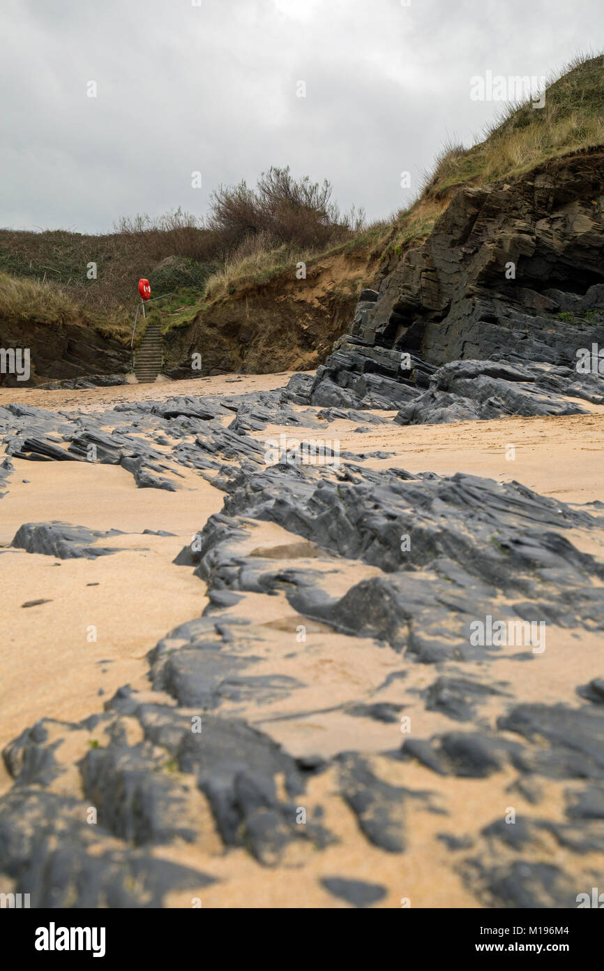 A view of a rocky Cornish beach with steps to a red life preserver belt ...