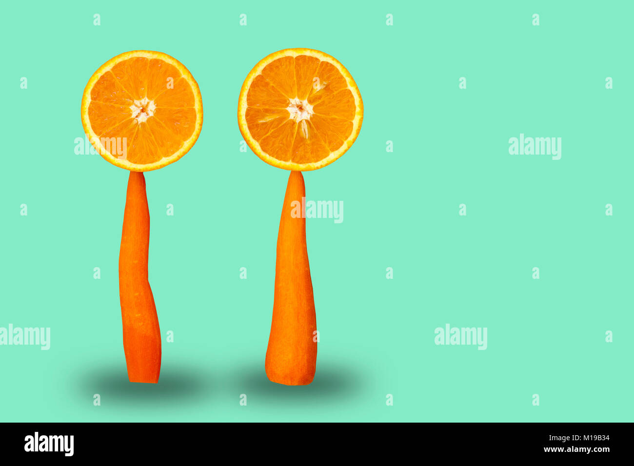 Two halfs of an orange and two carrots isolated on pastel green ...