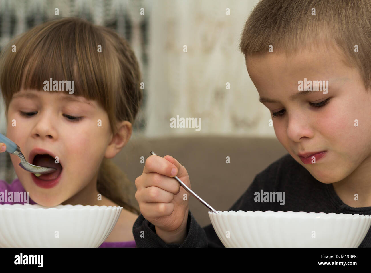 Two children boy and girl eating soup with spoon from a plate with open ...