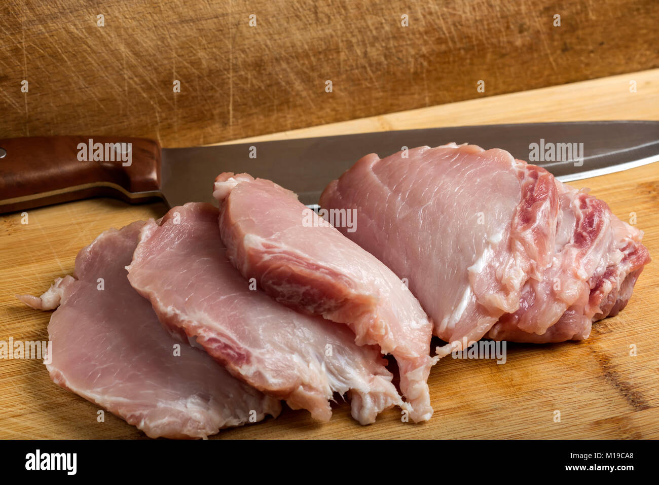 Slices of fresh pork sirloin meat with a kitchen knife on wooden ...