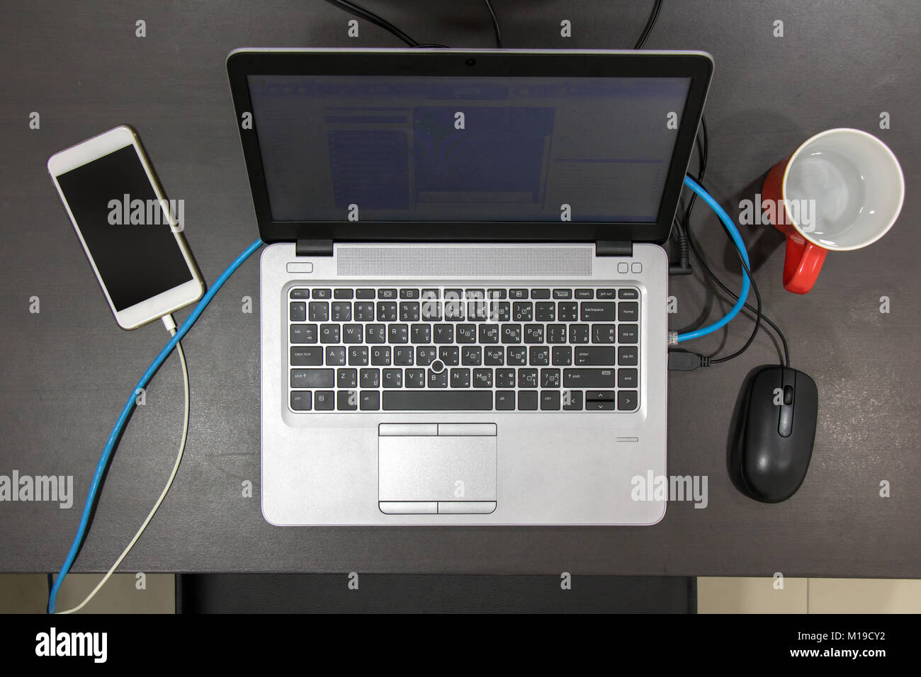 Notebook with smart phone and water in a cup on the desktop. Computer ...