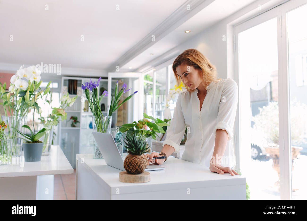 Woman flower shop owner using laptop computer at counter. Female ...