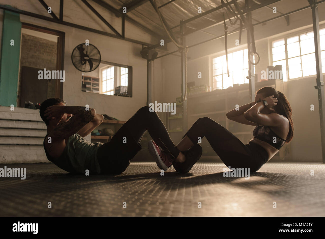 People working out in gym. Fit man and woman doing sit ups together ...
