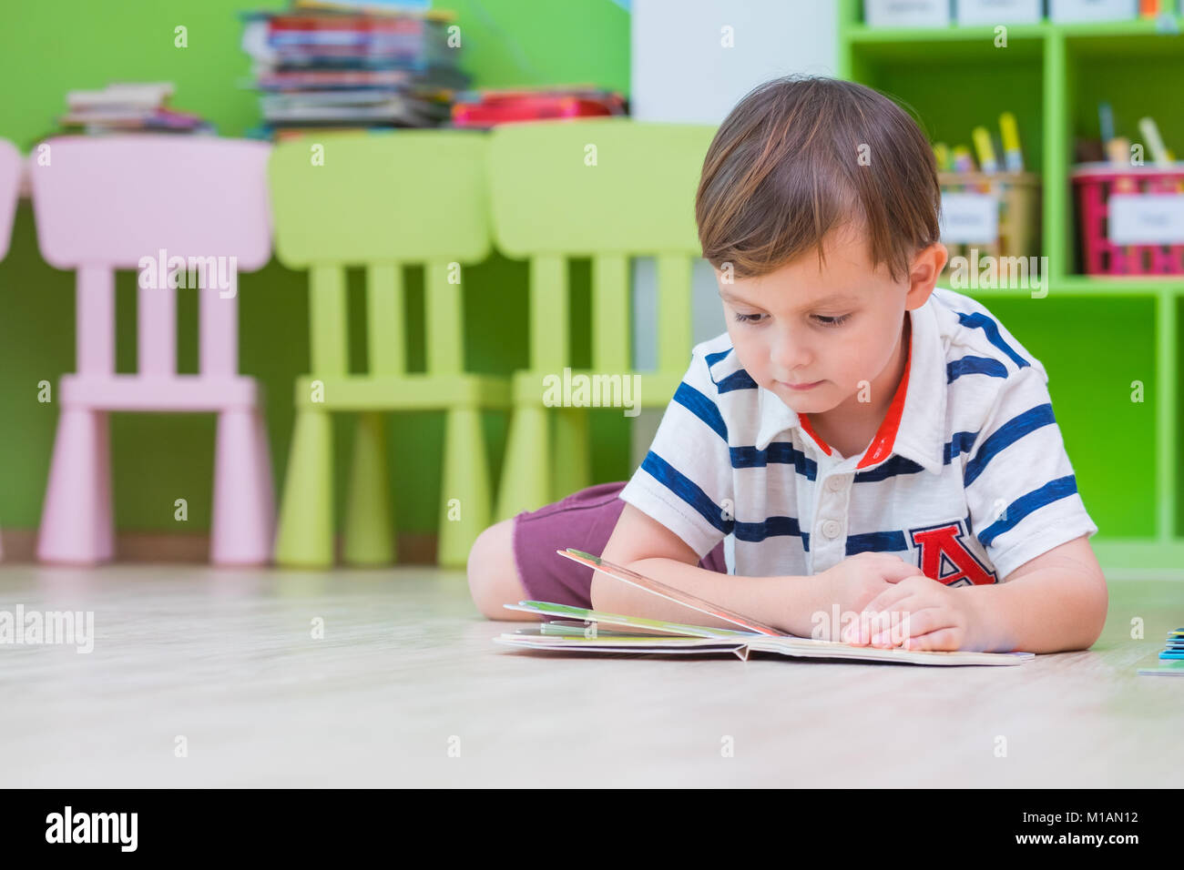 boy kid lay down on floor and reading tale book in preschool library ...