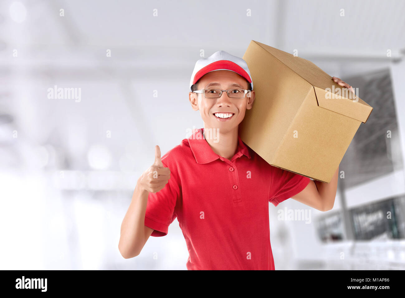 Smiling asian courier man with red uniform delivering parcel at indoors ...