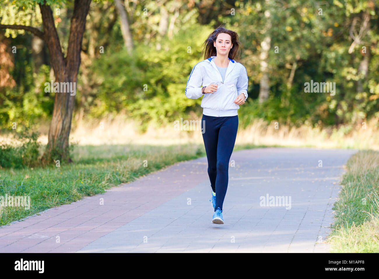 Young smiling sporty woman running in park in the morning. Fitness girl ...