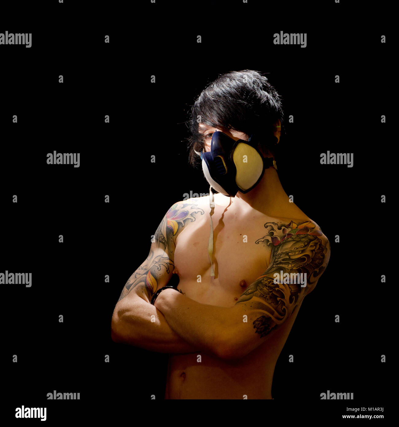 Young man with tattoos and wearing a face mask in a studio with black ...