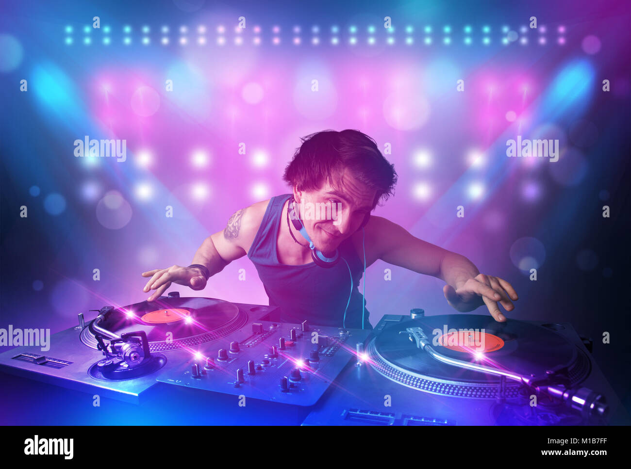 Young disc jockey mixing music on turntables on stage with lights and ...