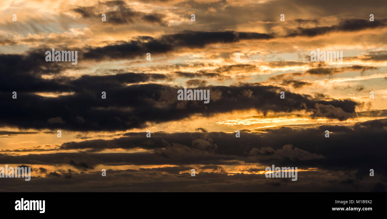 Orange rain clouds in the sky with dark blue clouds and sunbeams during ...