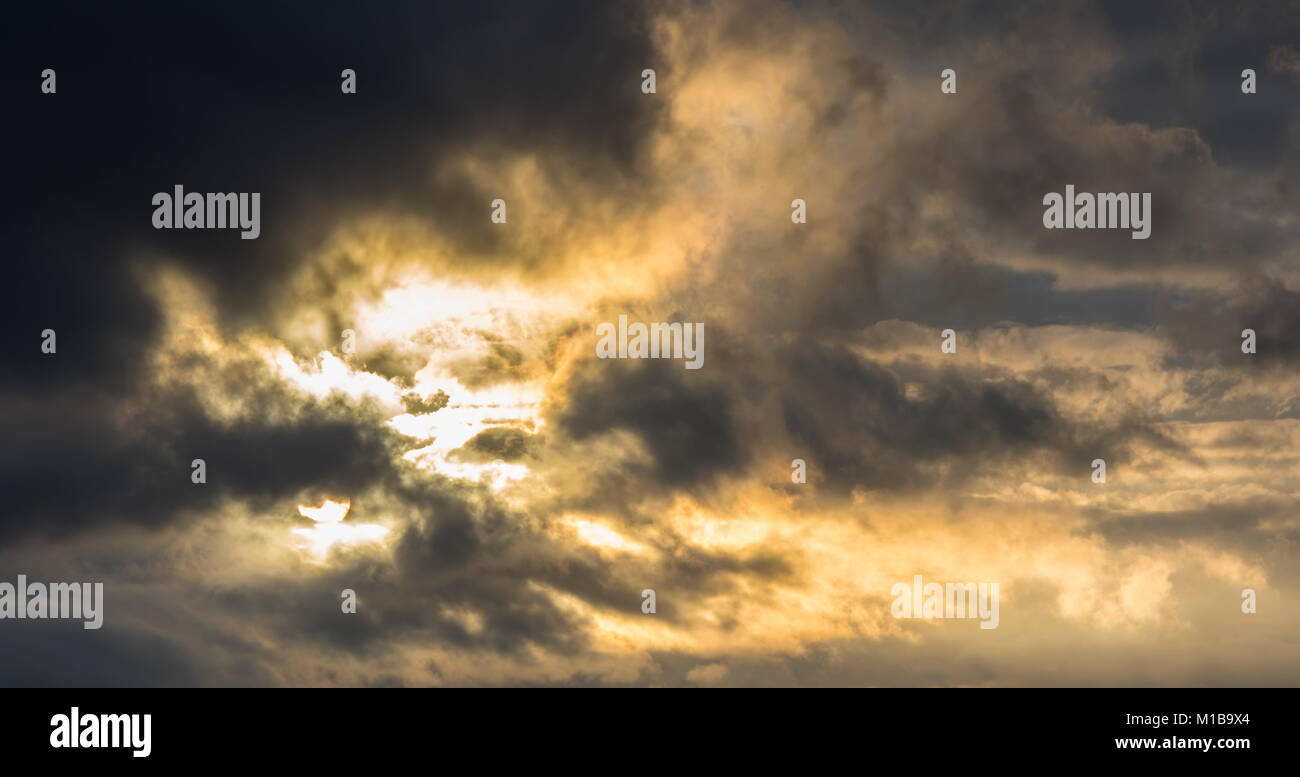 Orange rain clouds in the sky with dark blue clouds and sunbeams during ...