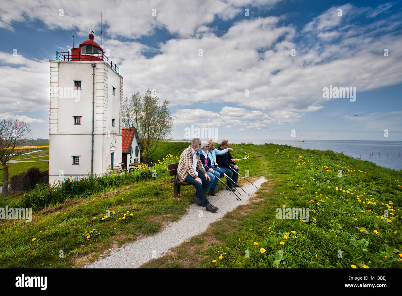 The Netherlands, Oosterdijk, Hikers on bench near former lighthouse at ...